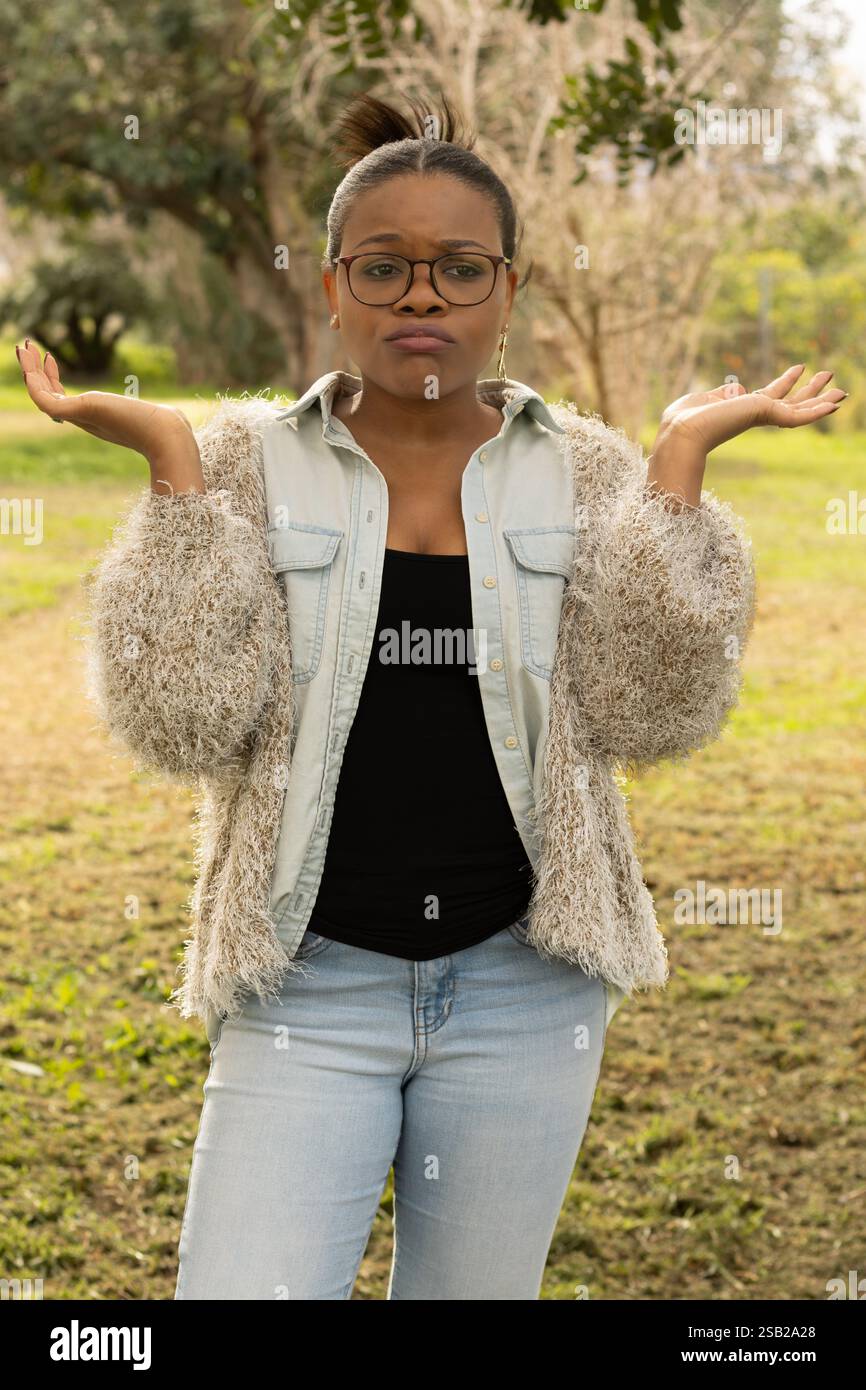 A young black woman wearing glasses and a stylish casual outfit shrugs ...