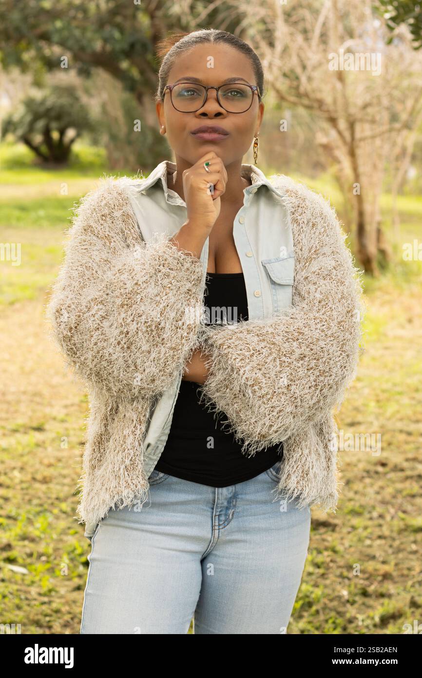 A black woman wearing glasses and a cozy outfit poses with a thoughtful ...