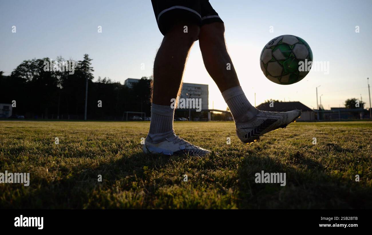 Legs of young man kicking ball at green field. Male feet of ...