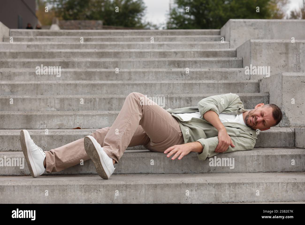 Man with injured arm on stairs outdoors after fall. Dangerous accident ...