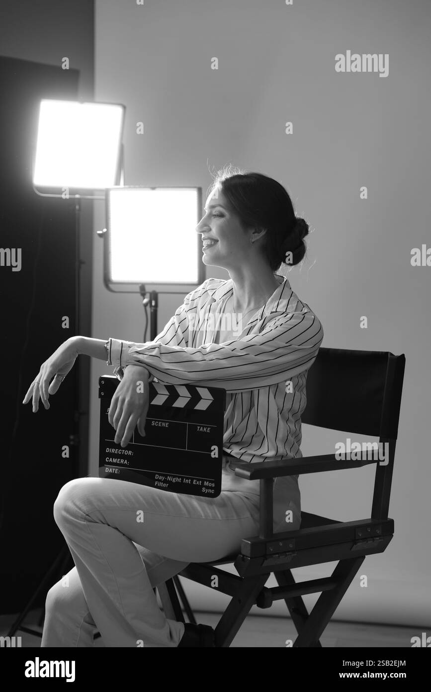 Beautiful woman with clapperboard sitting in director's chair in studio ...