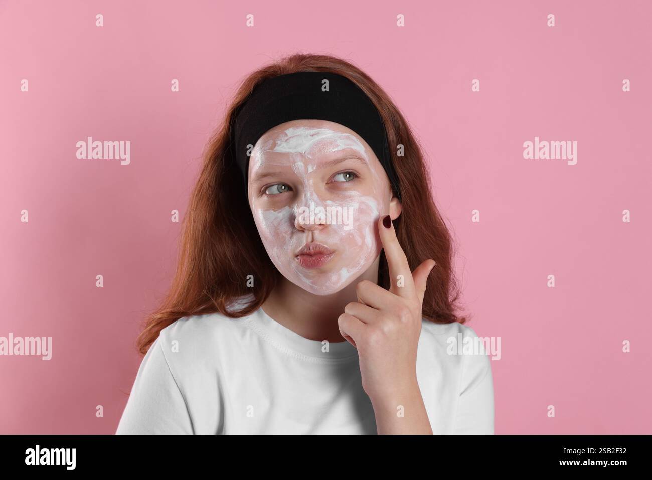 Teenage girl applying mask on her face with against pink background ...
