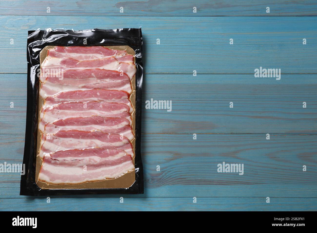 Pack of sliced bacon on light blue wooden table, top view. Space for ...