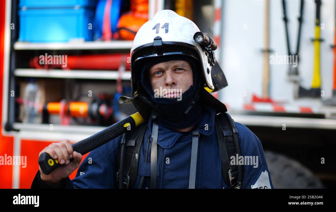 Portrait of confident male fireguard with axe standing near a fire ...