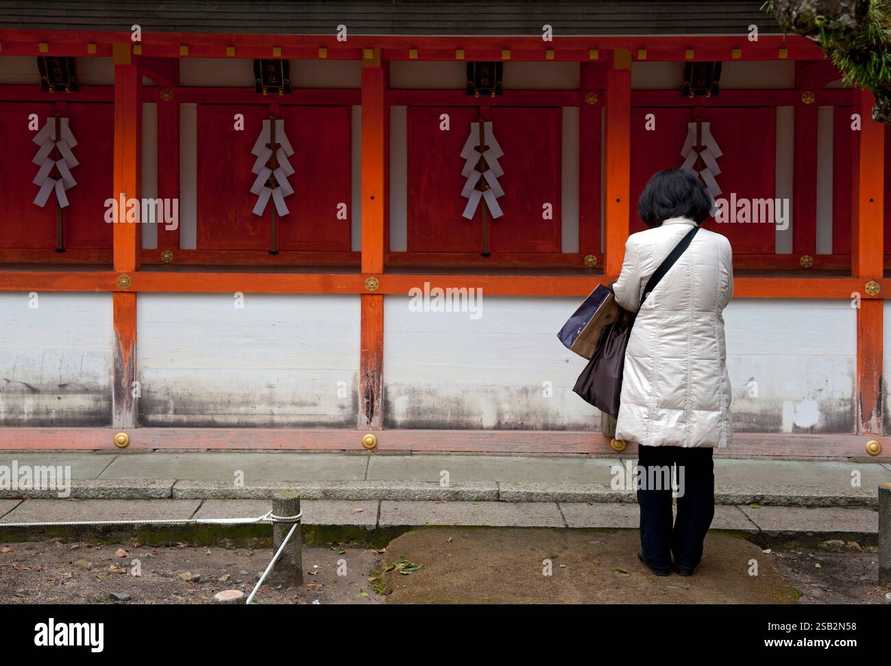 Woman praying at a mini shrine decorated with "shide" (zigzag white ...