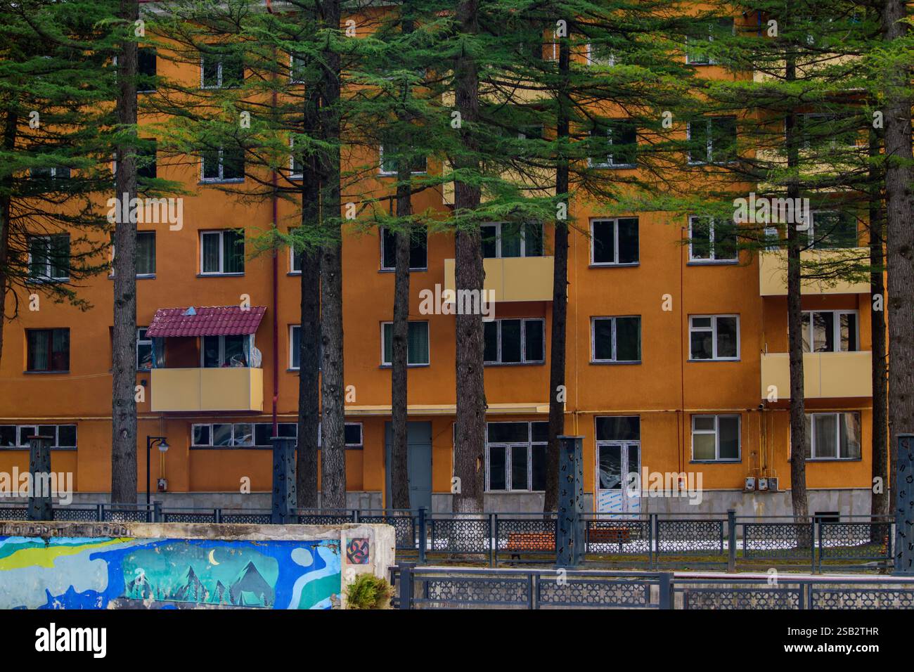A striking yellow building standing tall, with towering trees framing ...