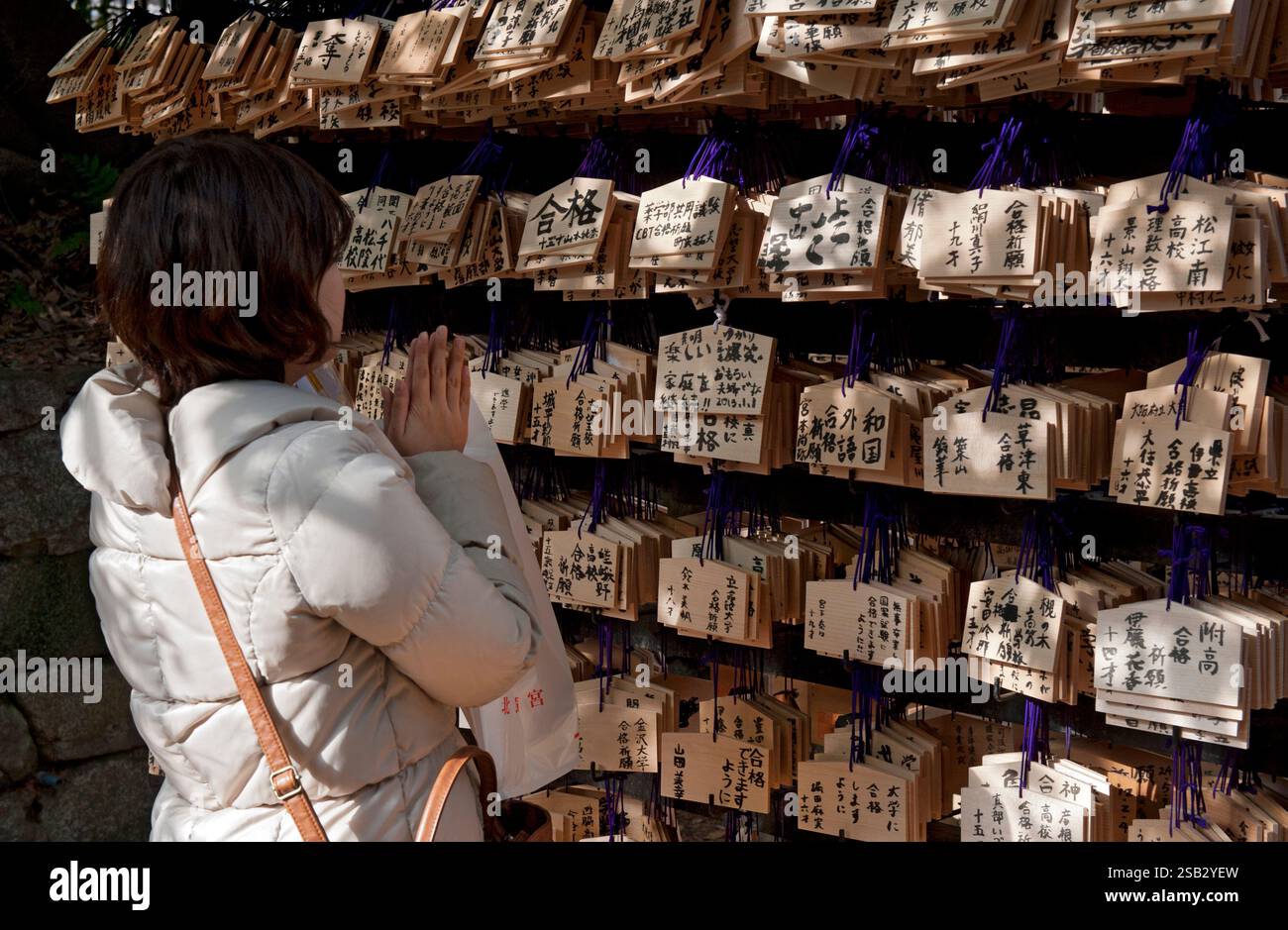 Woman praying in front of a collection of "ema" (wooden prayer plaques ...