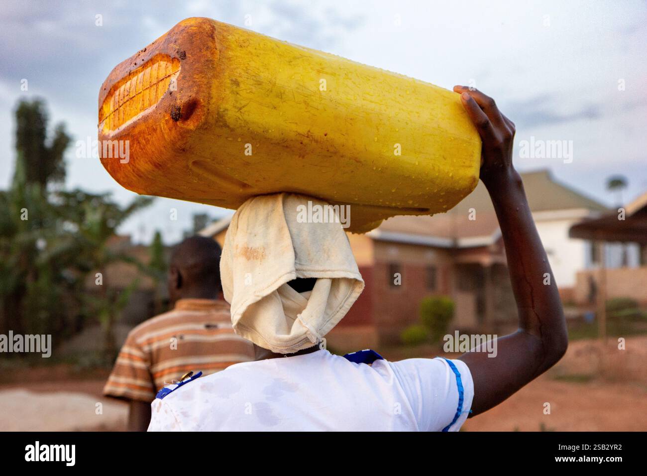 A woman carrying home a jerrycan full of water from a nearby water ...