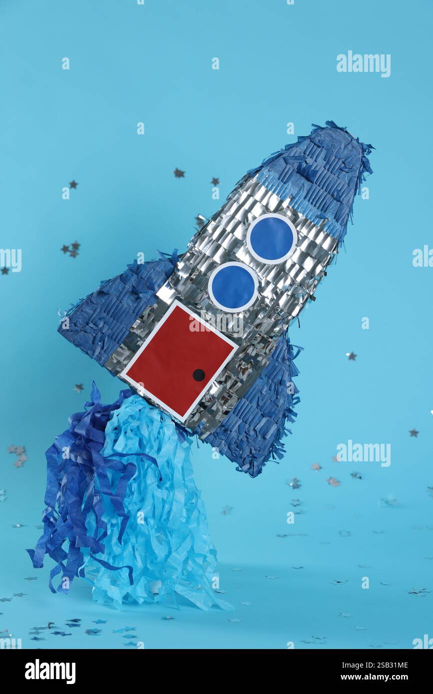 Rocket shaped pinata and confetti on light blue background Stock Photo ...