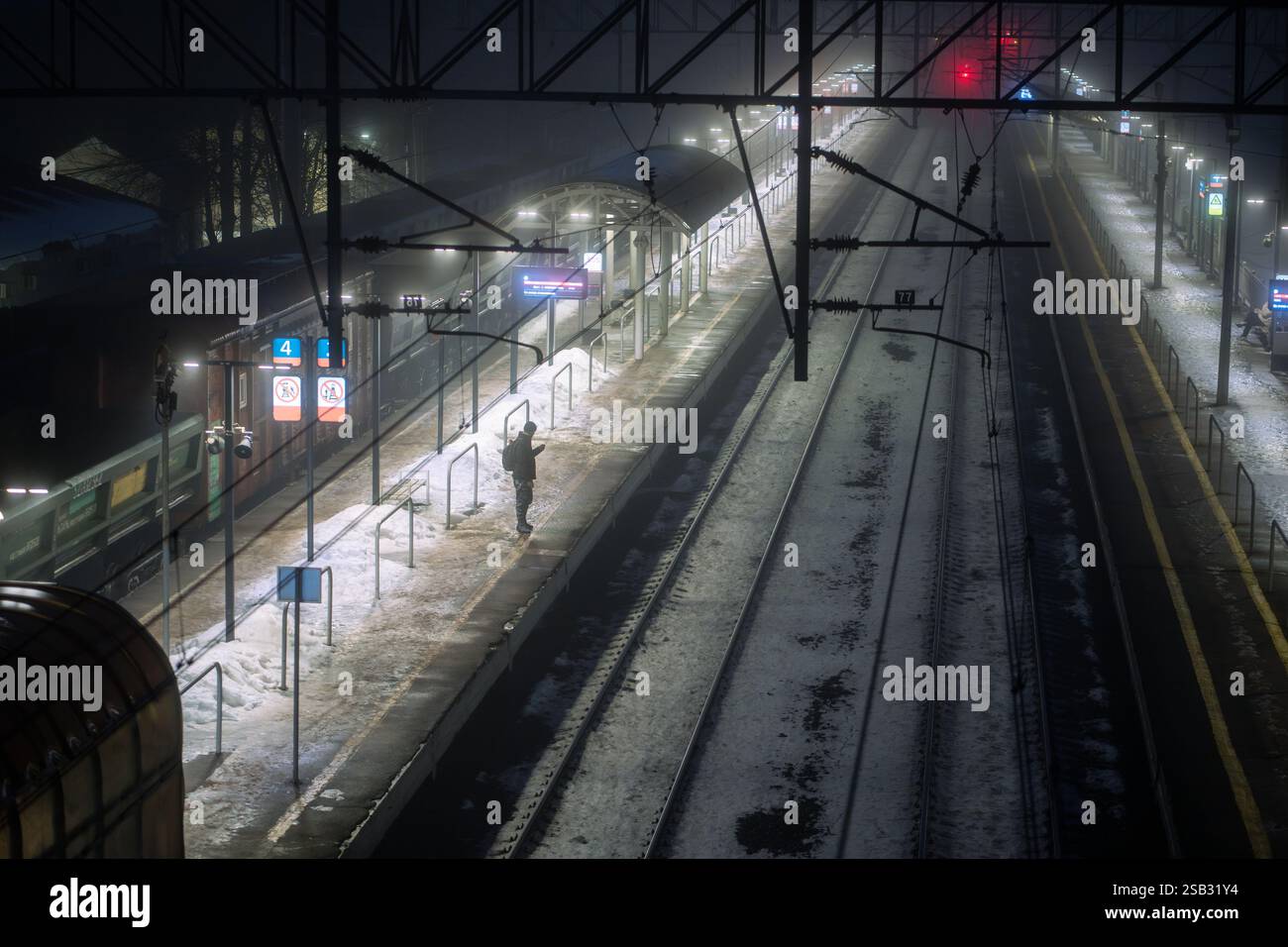 Single man stands wait train under winter night sky, fog with cold damp ...