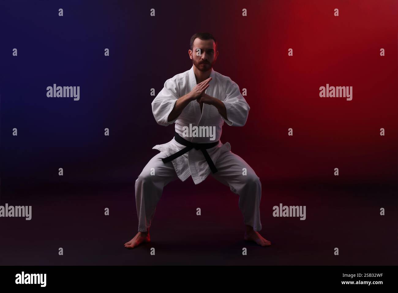 Man wearing uniform practicing karate in color lights against black ...