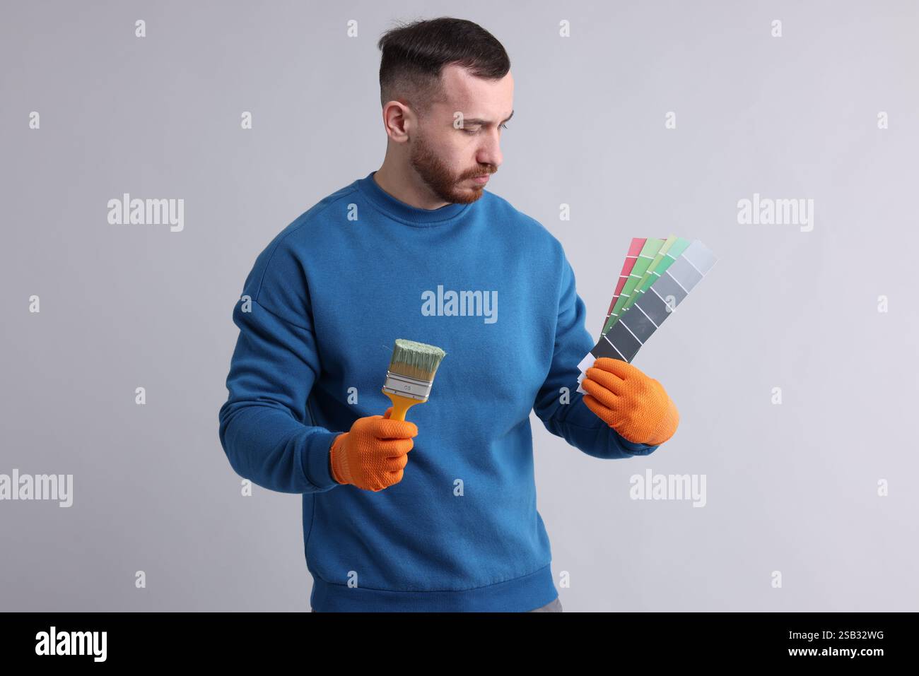 Man with paintbrush and color selection chart on light grey background ...