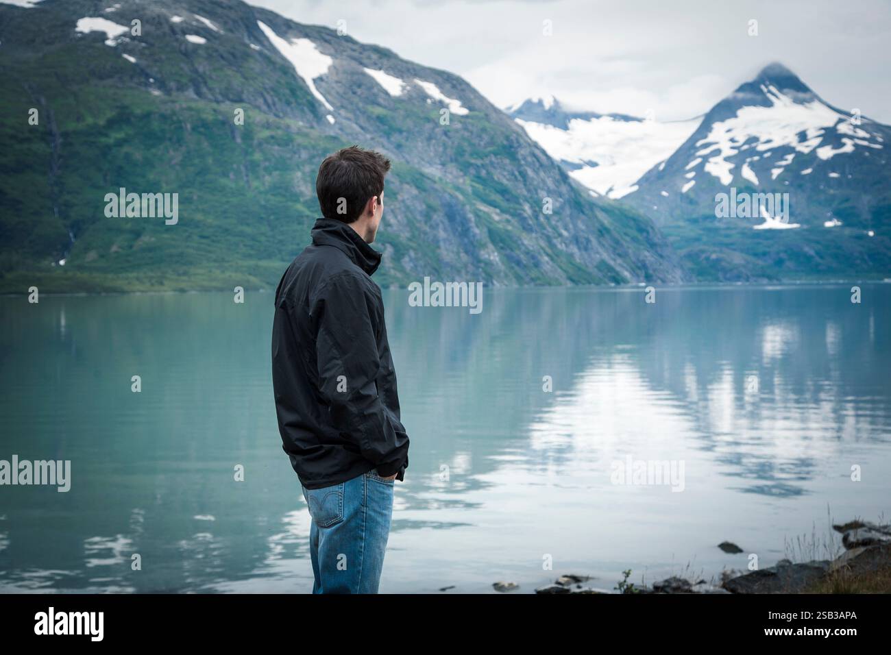 Toned photo of a young man contemplating a lake and mountains in Alaska ...