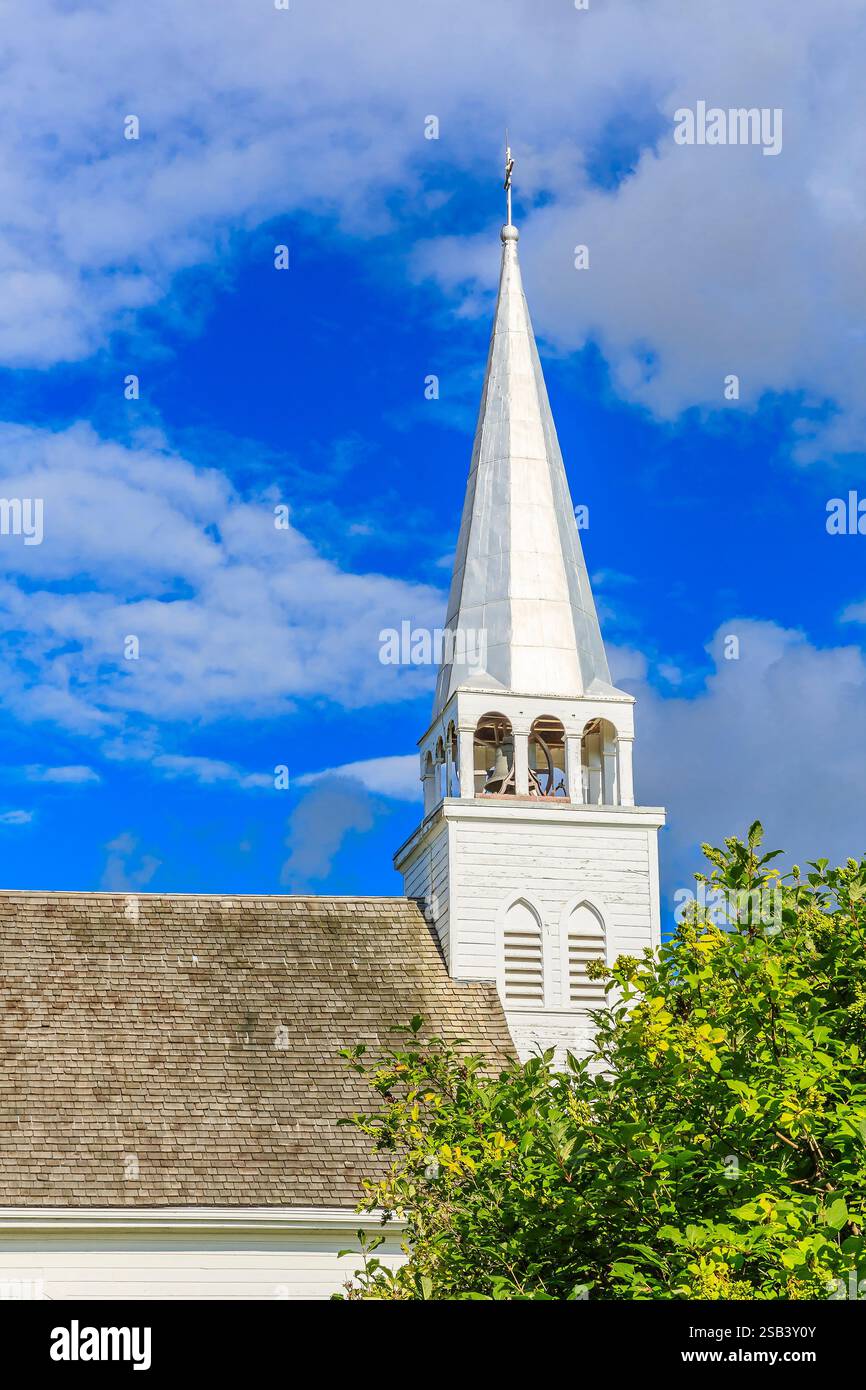 A white church steeple with a cross on top. The sky is blue and there ...