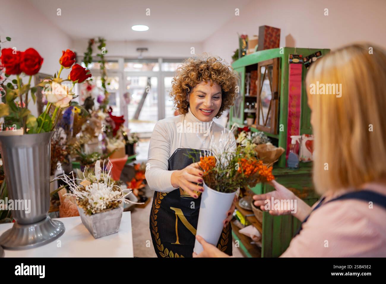 Inside a cozy flower shop, a smiling florist hands a vibrant bouquet to ...