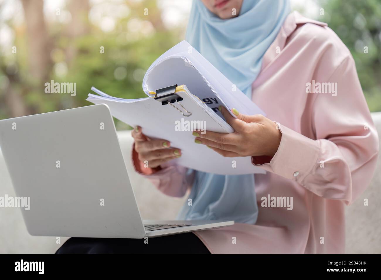 Muslim business woman in hijab reviewing documents next to a laptop outdoors Stock Photo - Alamy