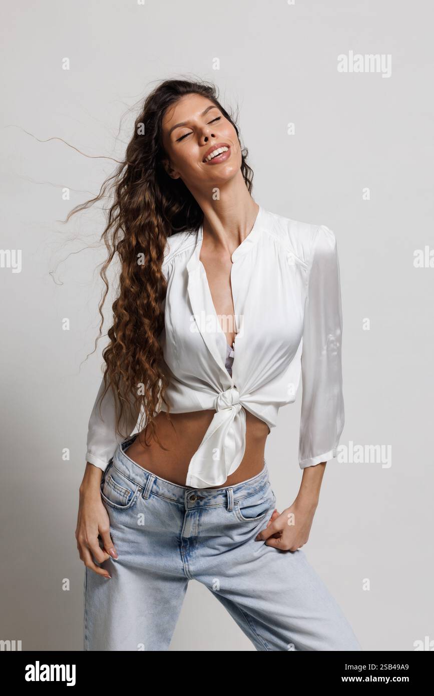 A confident woman poses in a relaxed style, wearing a white knotted top ...