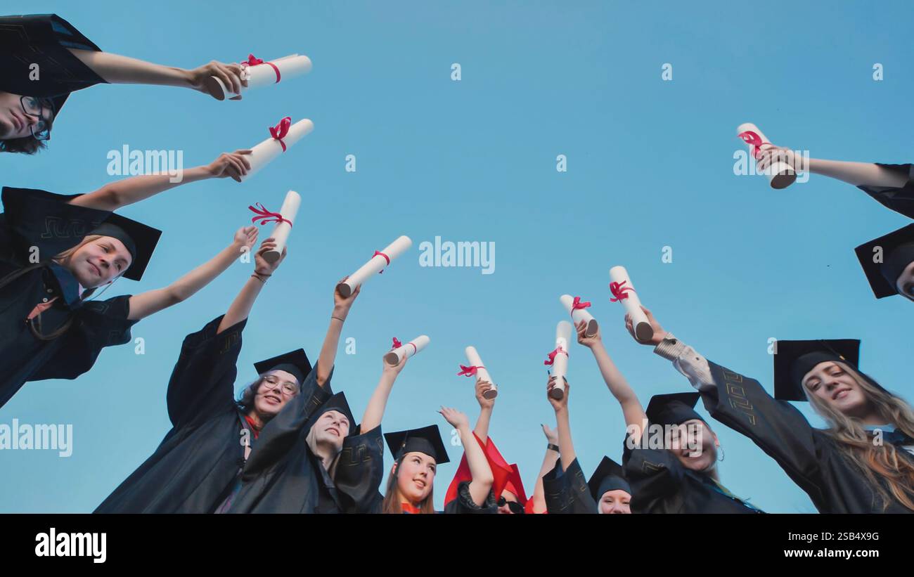 Students in graduation attire celebrating their achievement by raising ...