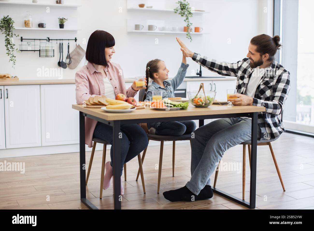 Caucasian family enjoying breakfast together. Young daughter gives high ...
