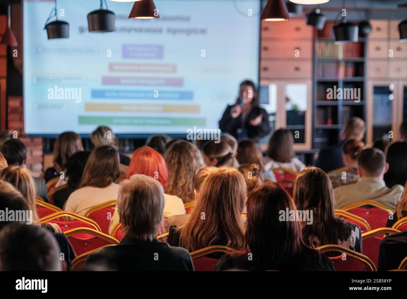 A diverse audience listens to a speaker giving a presentation in a ...
