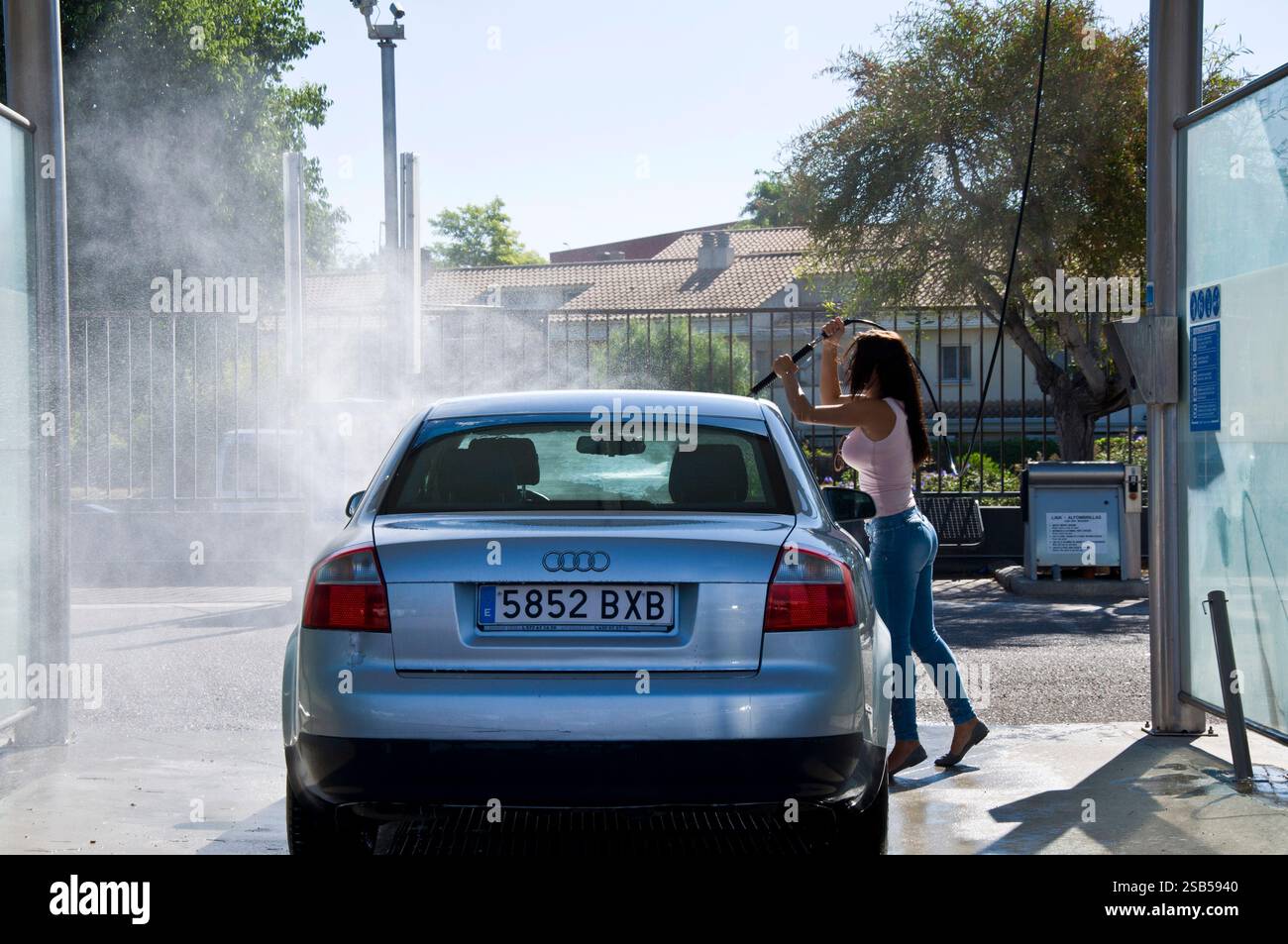 Cute young woman washing the car in a petrol station with car wash ...