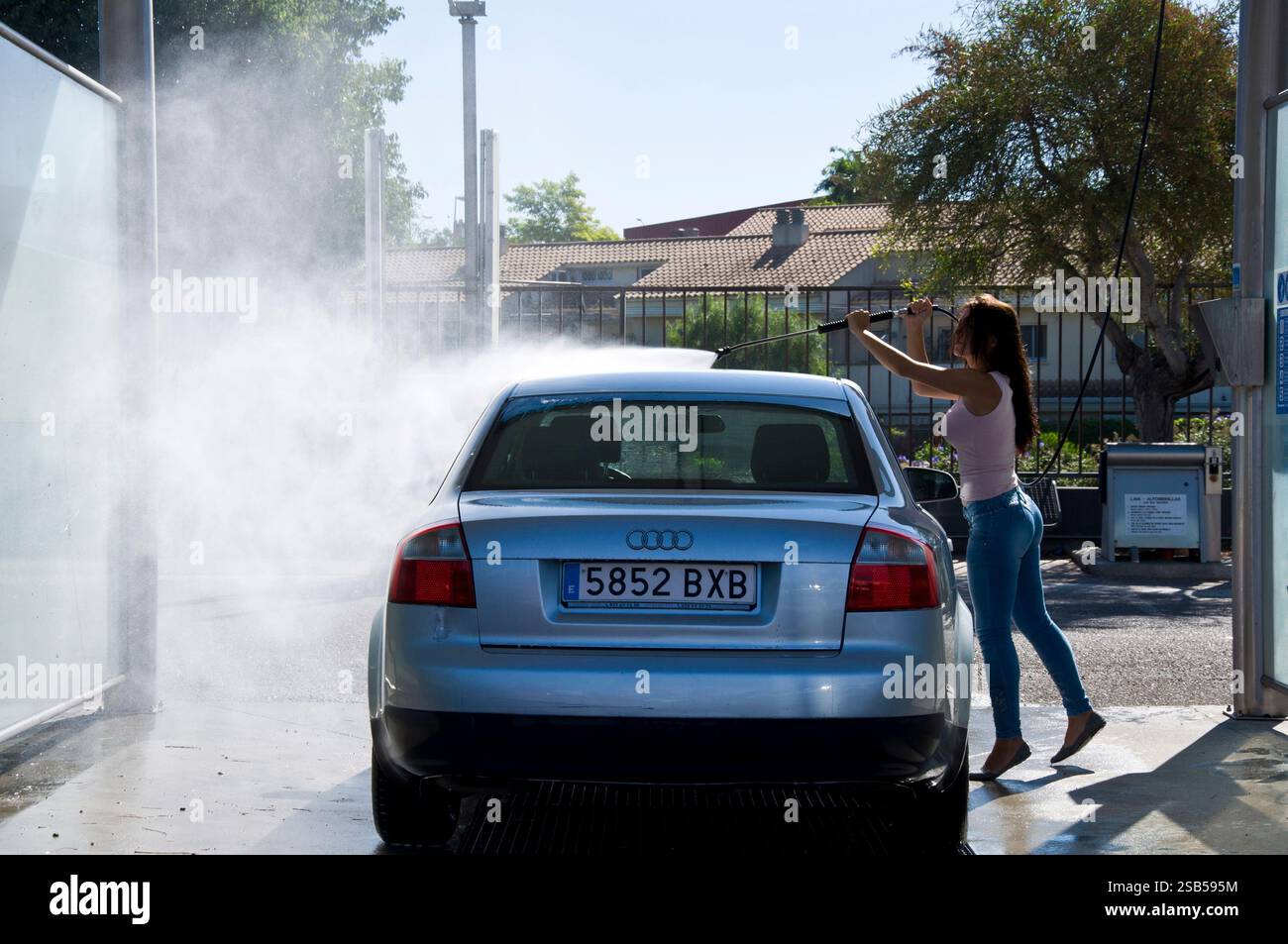 Cute young woman washing the car in a petrol station with car wash ...