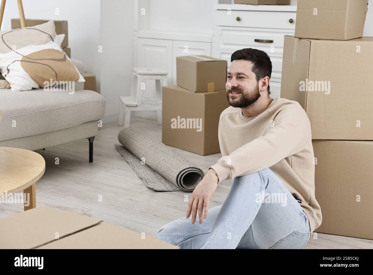 Moving day. Man resting on floor near cardboard boxes in his new home ...
