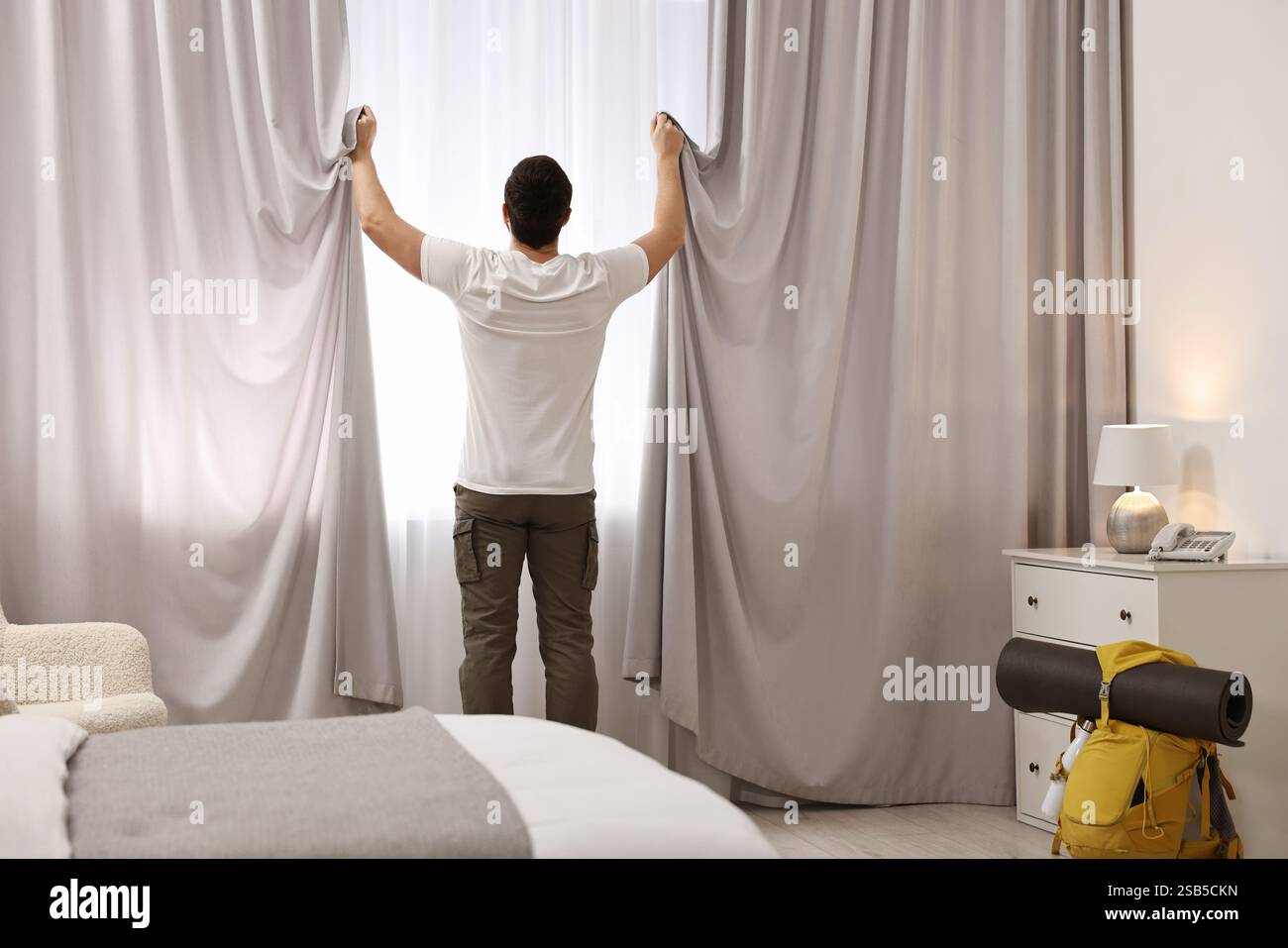 Traveller opening curtains in hotel room, back view Stock Photo - Alamy