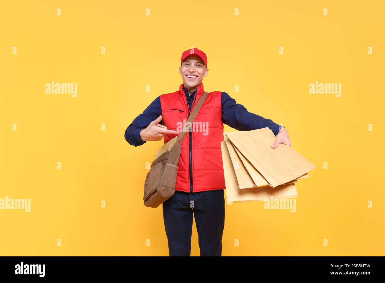 Happy postman with bag pointing at envelopes on yellow background Stock ...