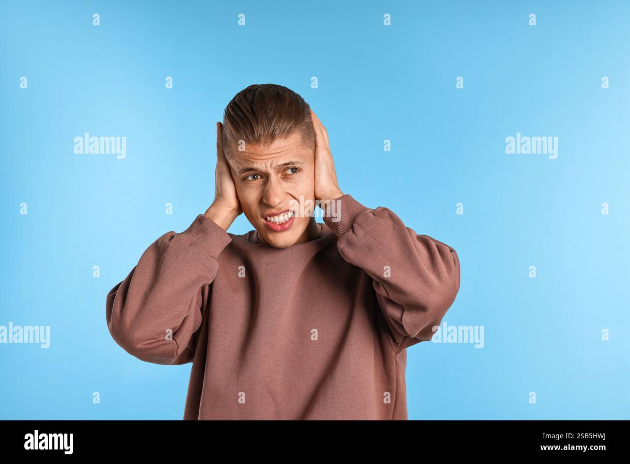 Annoyed young man covering his ears due to loud sound on light blue background Stock Photo - Alamy