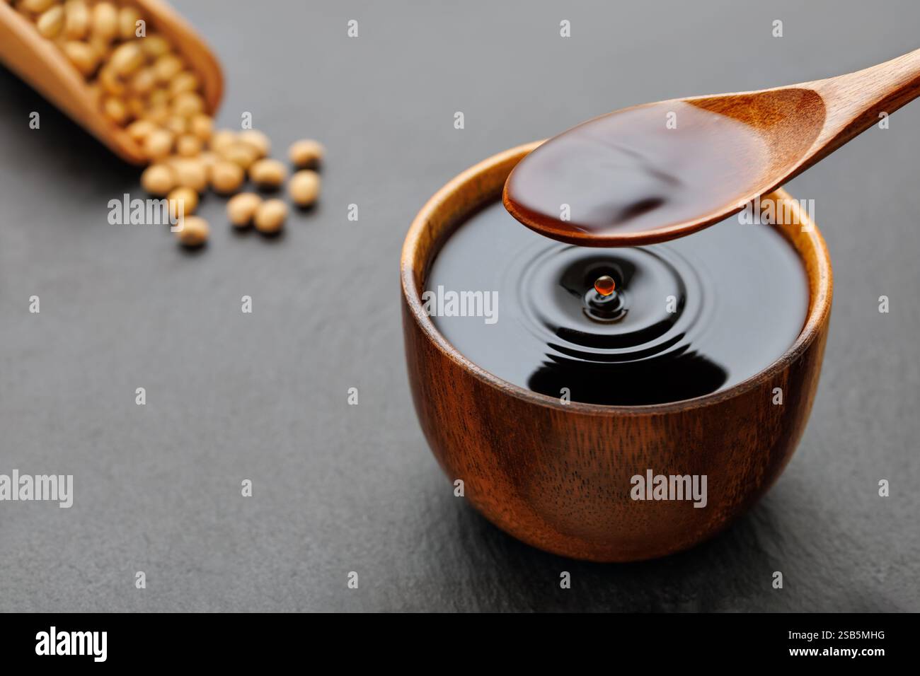 soy sauce pouring from spoon in wooden bowl with splash and drop and ...