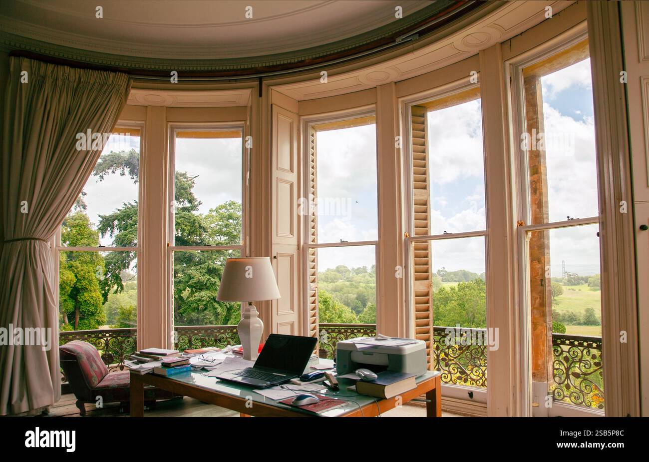 A large bay window overlooking rolling hilsl from a desk in a study ...
