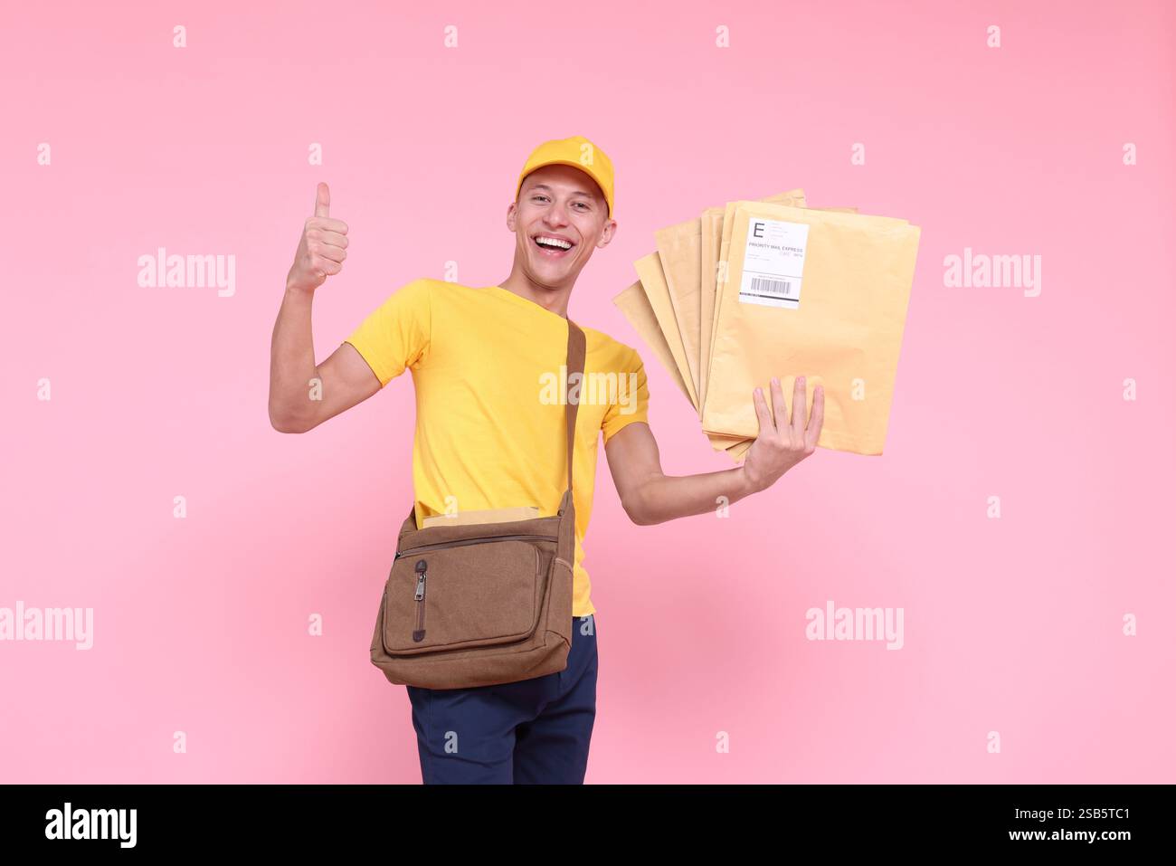 Happy postman with bag and envelopes showing thumbs up on pink ...