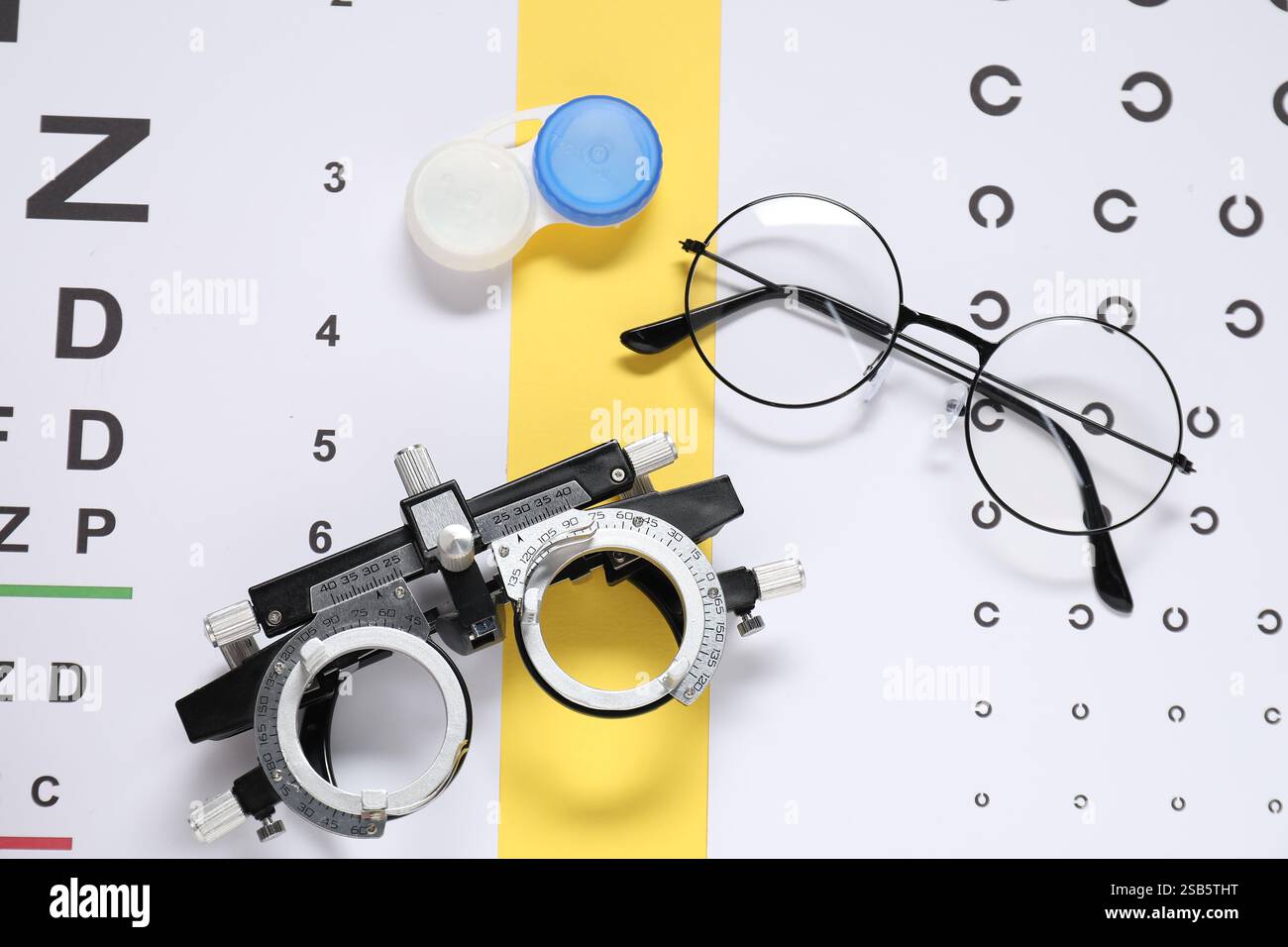 Glasses, trial frame, vision test charts and lenses on yellow ...
