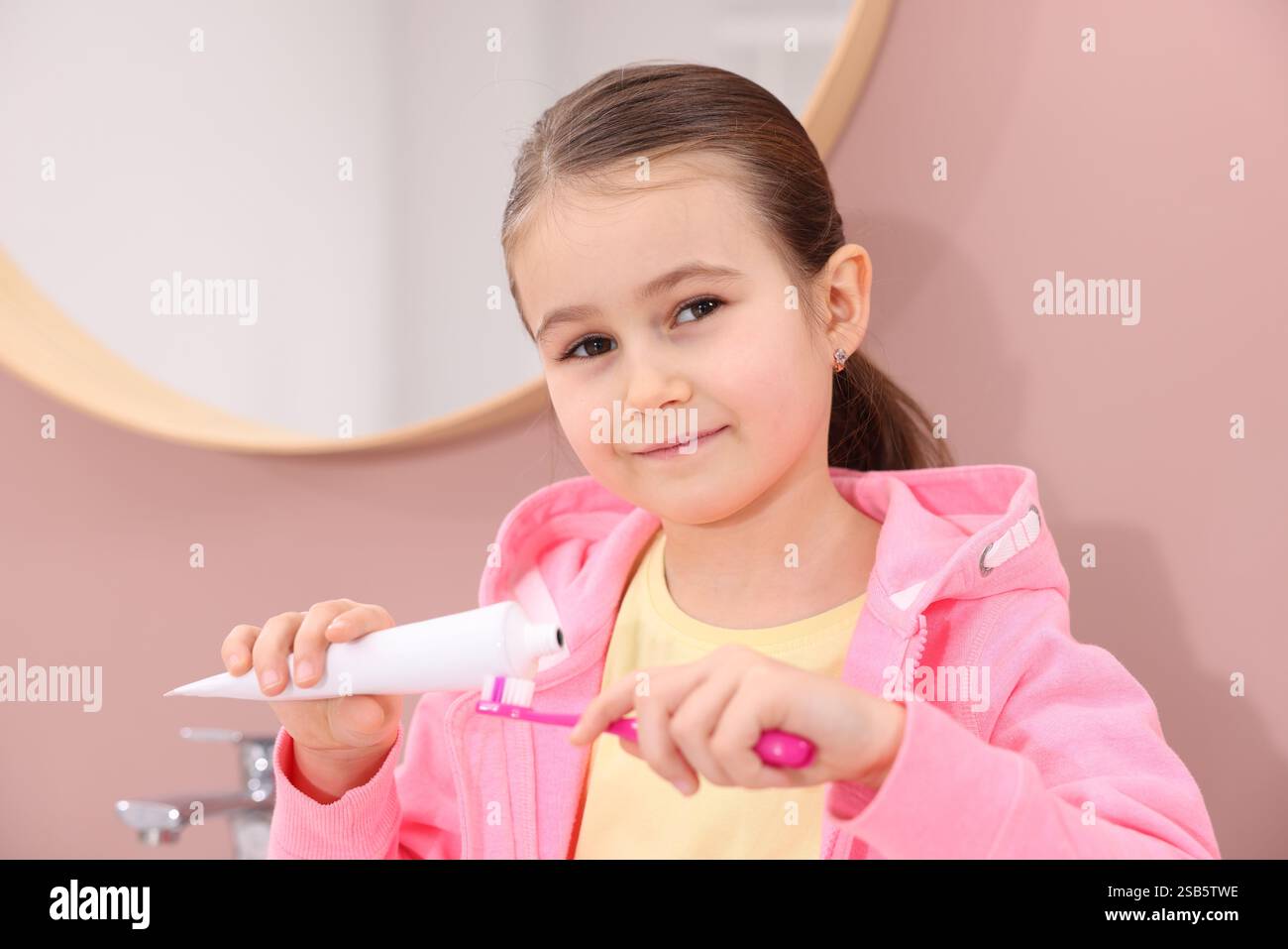 Cute girl applying toothpaste onto toothbrush in bathroom Stock Photo ...