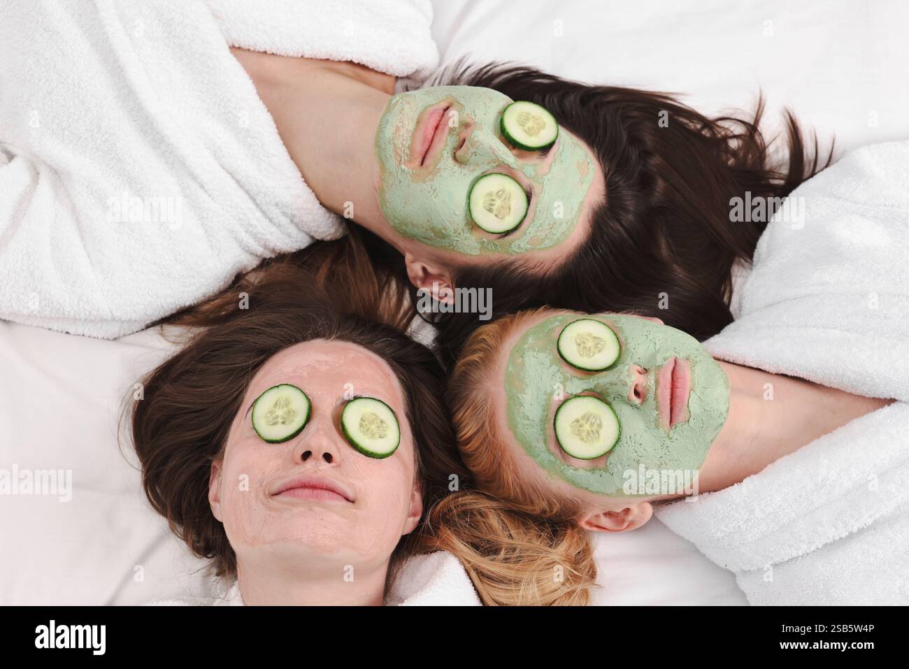 Spa day. Beautiful woman with face masks and cucumber slices on bed ...