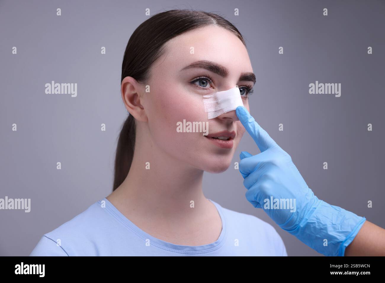 Doctor checking patient's nose after plastic surgery operation on grey ...