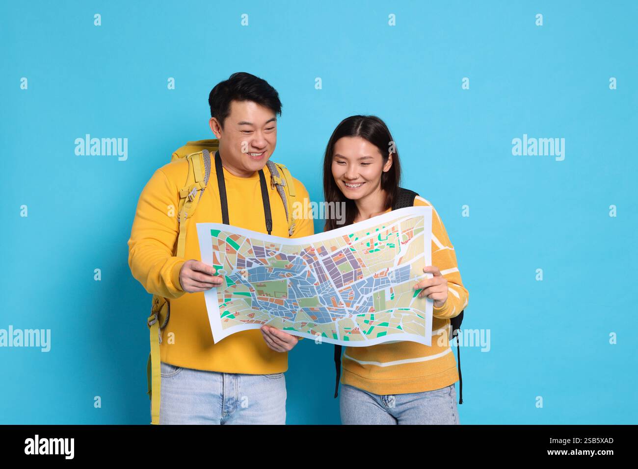 Happy travellers with map on light blue background Stock Photo - Alamy