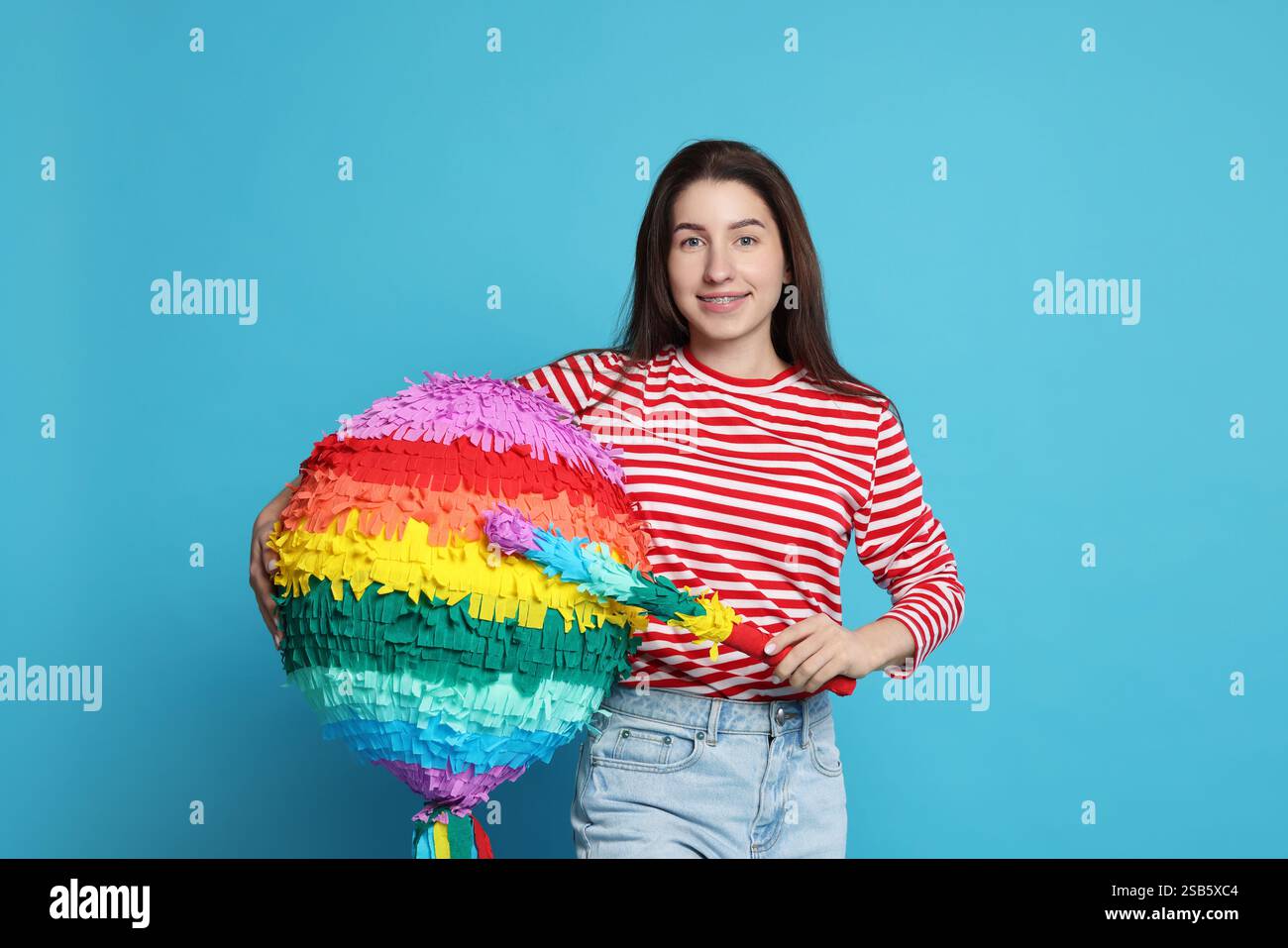 Happy woman with colorful pinata and stick on light blue background ...