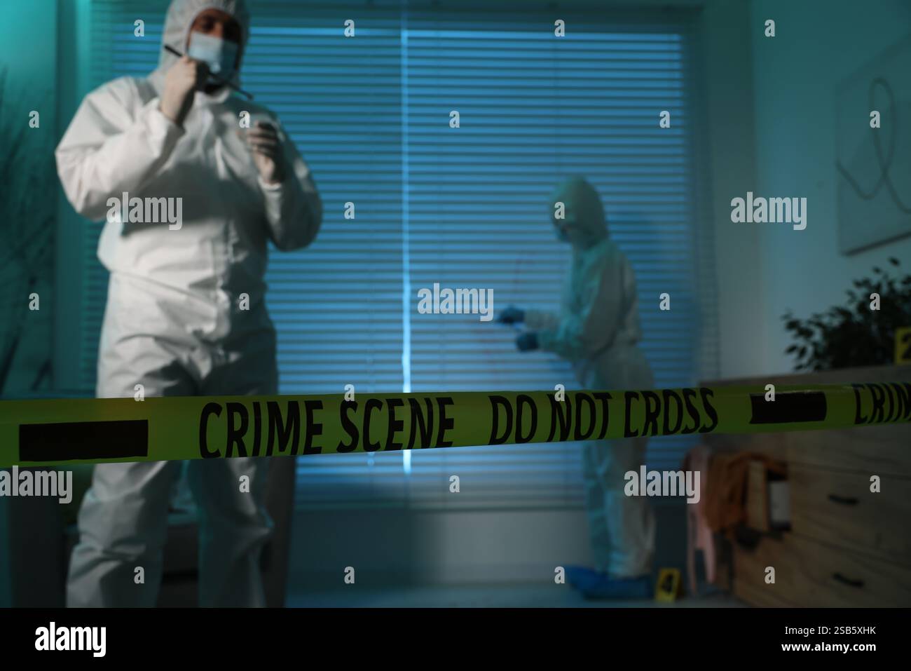 Forensic experts working at crime scene indoors, focus on yellow tape ...