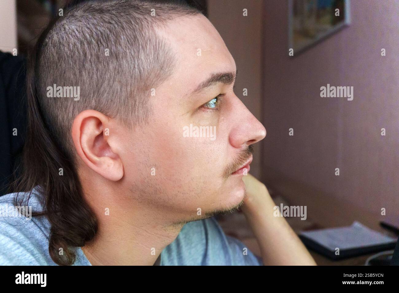 A man with a distinctive half-shaved hairstyle gazes thoughtfully to ...