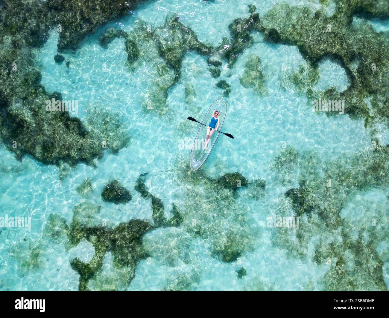 Aerial view of a woman reclining in a transparent kayak floating over ...