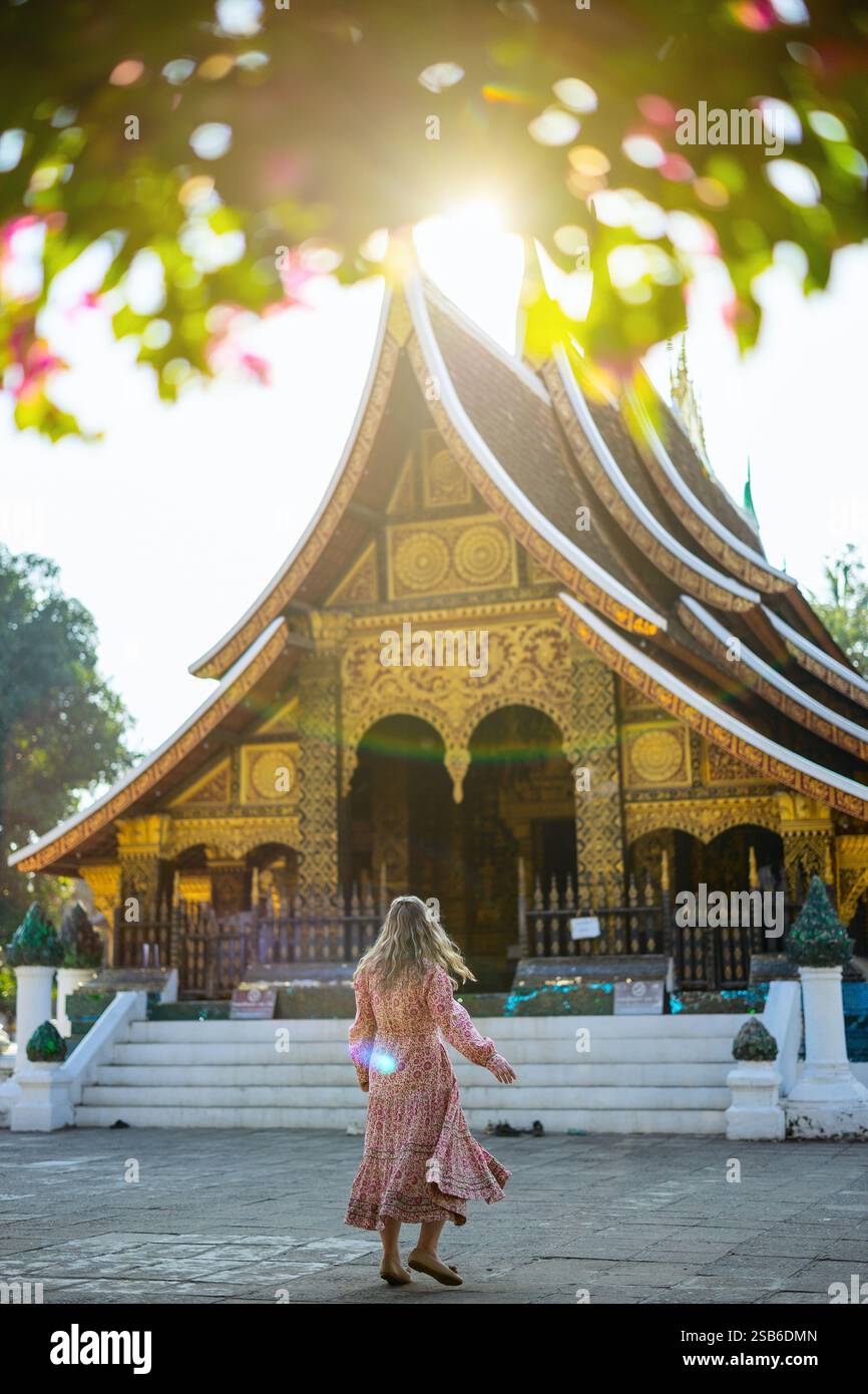 A woman in traditional attire approaches the golden Wat Xiengthong ...