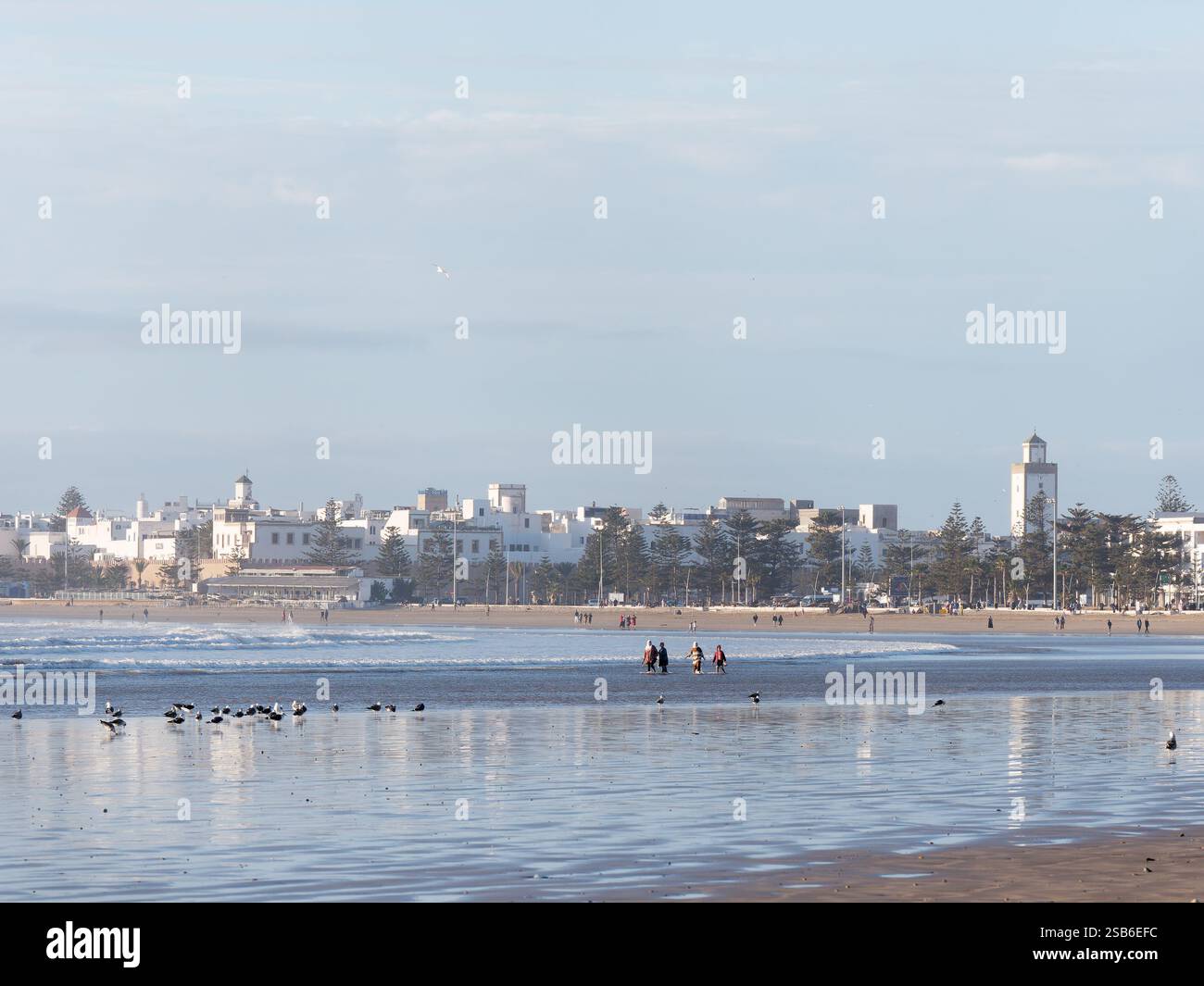 People walk along the shallow shoreline on a sandy beach with historic ...