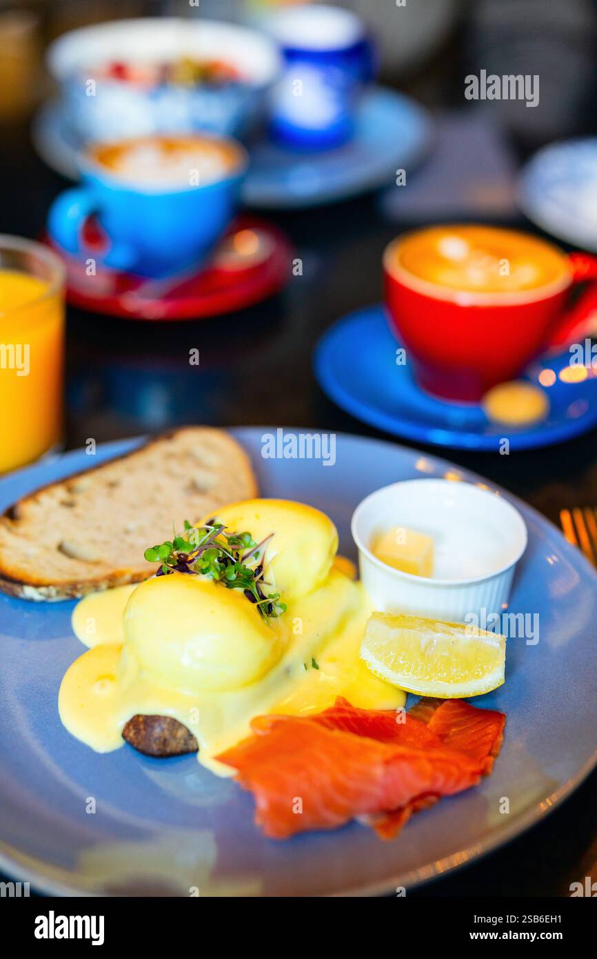 A breakfast plate featuring Eggs Benedict topped with hollandaise sauce ...
