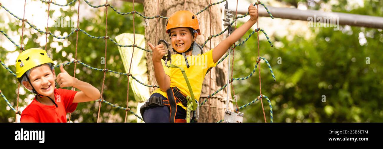Small children climb a rope bridge in a rope park. Children are having ...