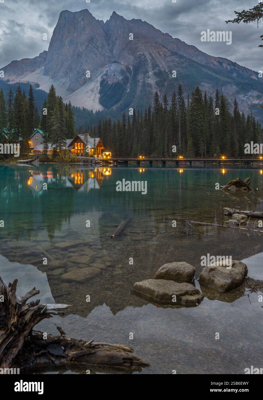 Emerald Lake in Canada, with a cozy lakeside cabin glowing at twilight, surrounded by lush ...