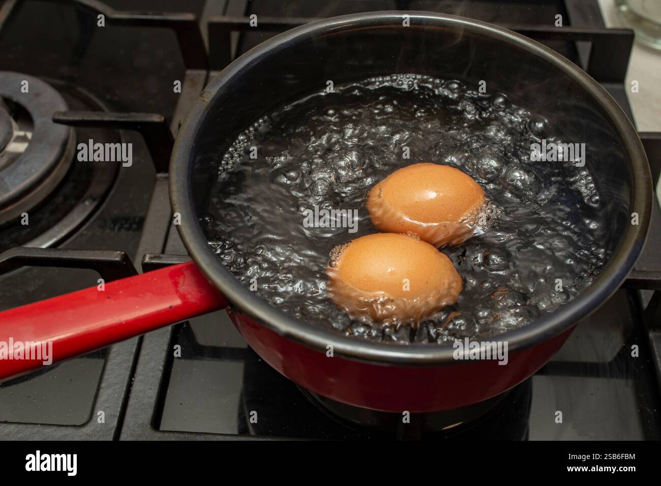 Two orange eggs boiling in a black pot with bubbles and steam, soft ...
