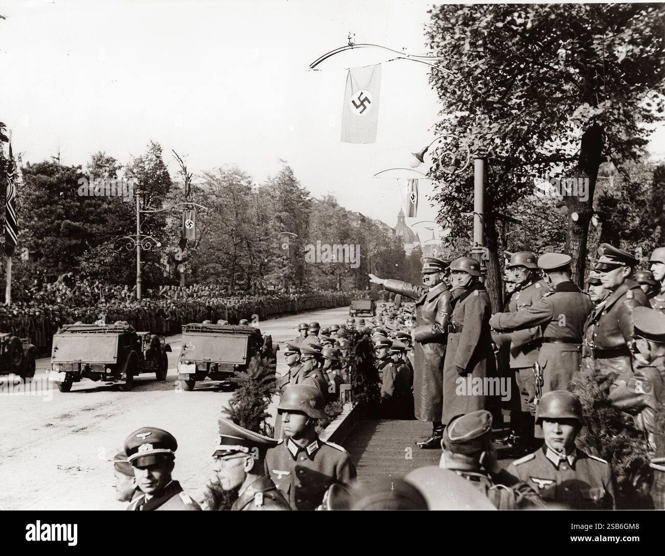 Adolf Hitler (right, saluting) salutes as a parade of vehicles and ...