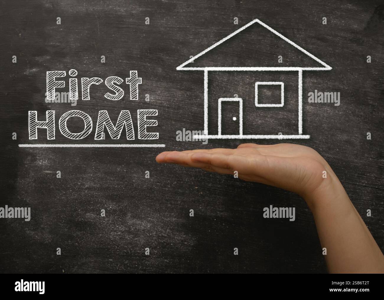 Hand holding a chalkboard with the words First Home written on it. The ...